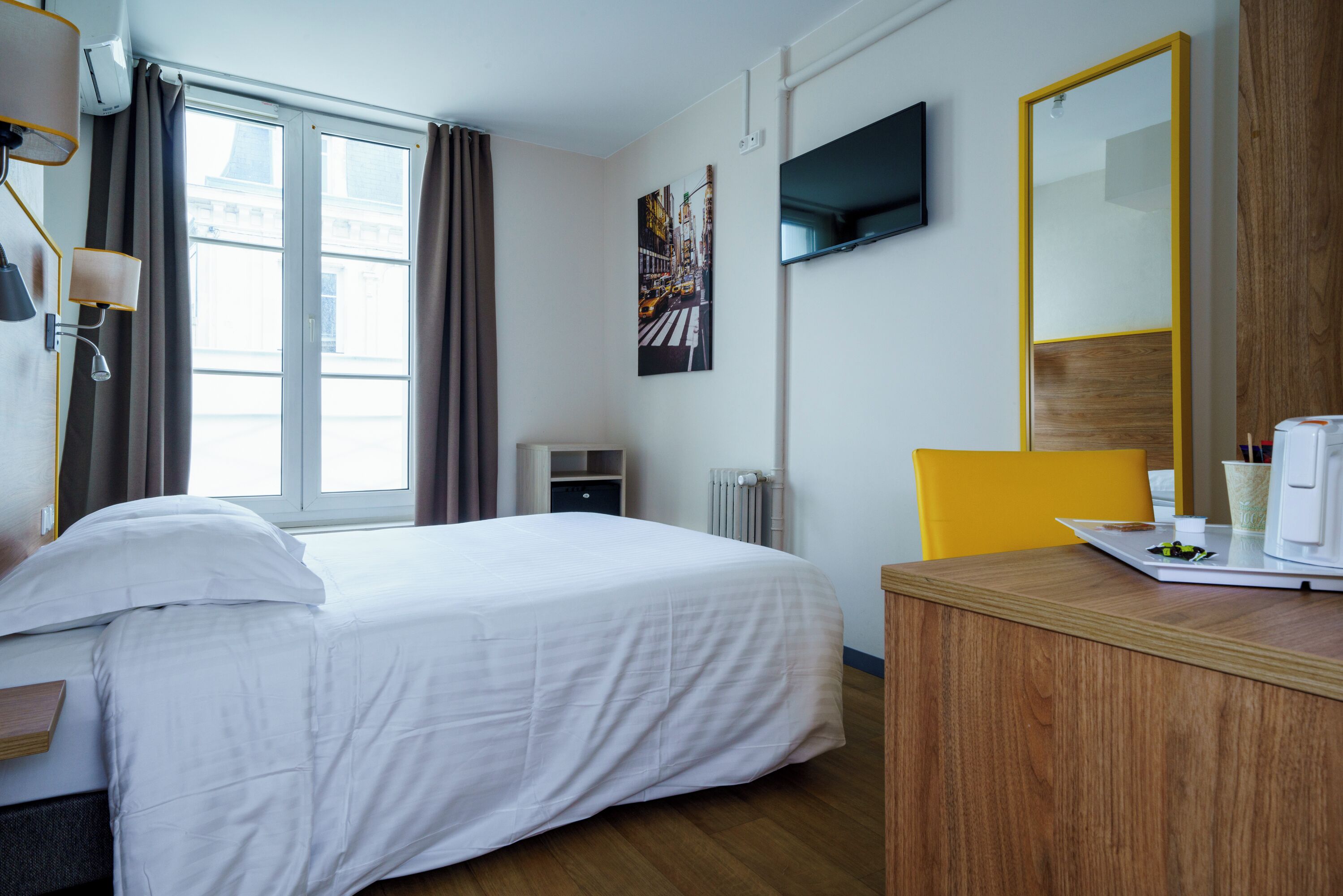 Quarto de hotel com cama, escrivaninha com cadeira, televisão de tela plana e um espelho grande.