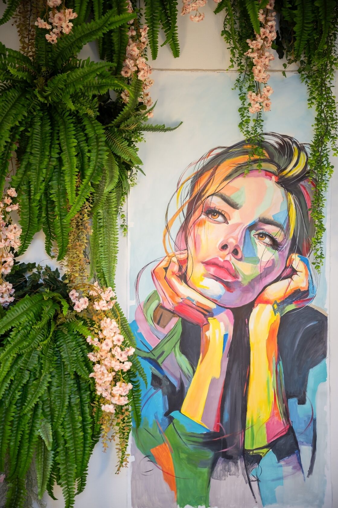 Uma pintura vibrante mostrando uma pessoa, rodeada por samambaias verdes exuberantes e flores cor-de-rosa.