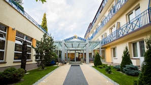 Entrada de hotel com galeria coberta, portas de vidro e uma estátua.