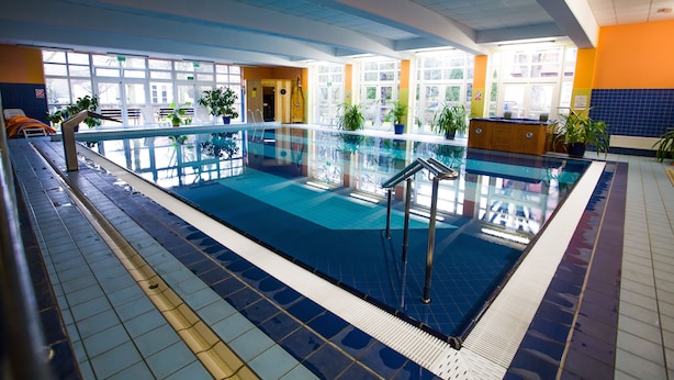 Piscina interna com água cristalina, piso azulejado e cadeira do salva-vidas.