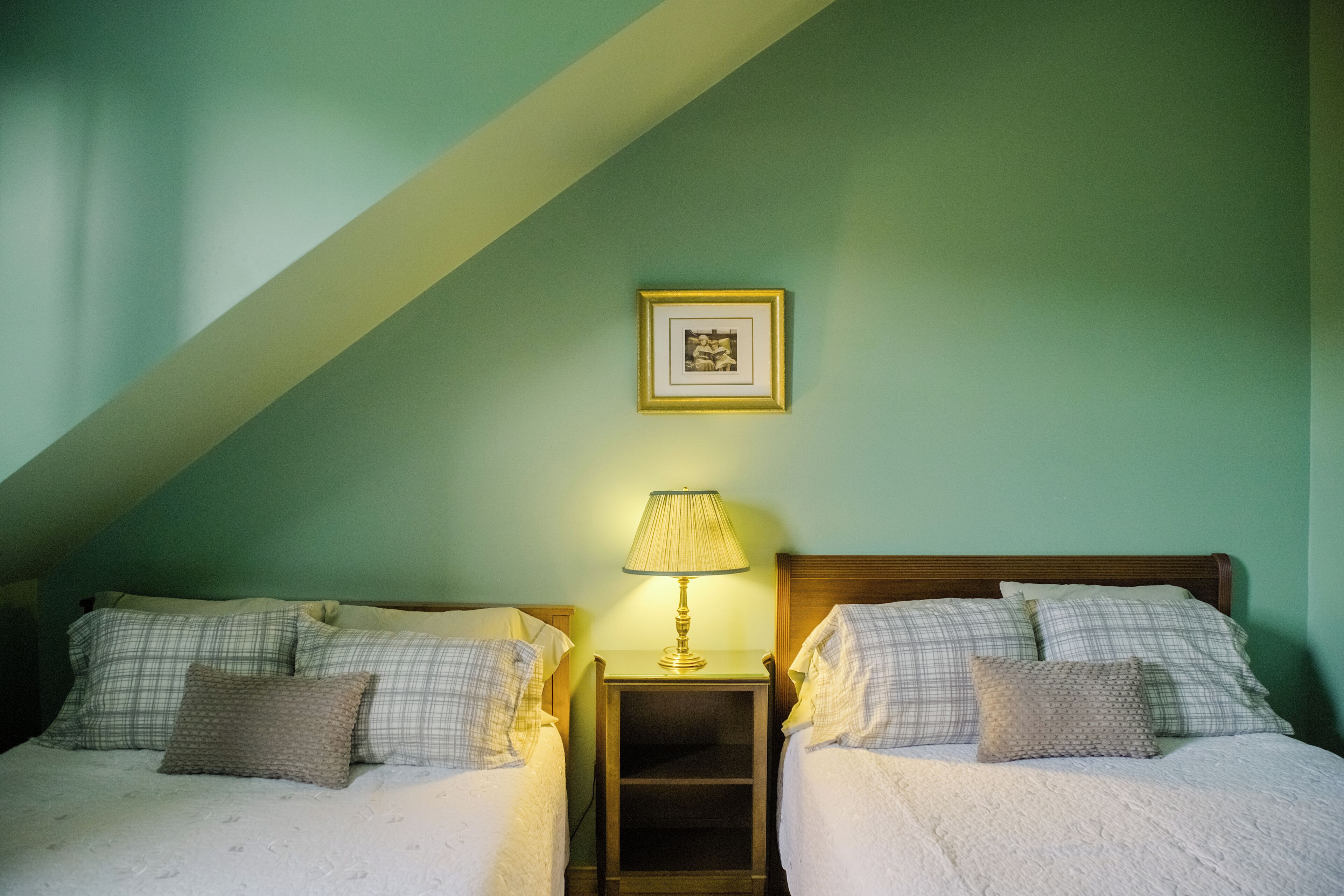 Quarto com duas camas, uma mesa de cabeceira com abajur e um quadro na parede.