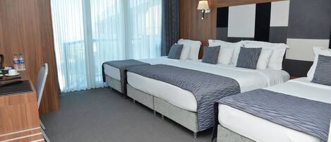 Quarto de hotel com duas camas, uma escrivaninha e uma cadeira. Há garrafas de água na escrivaninha.