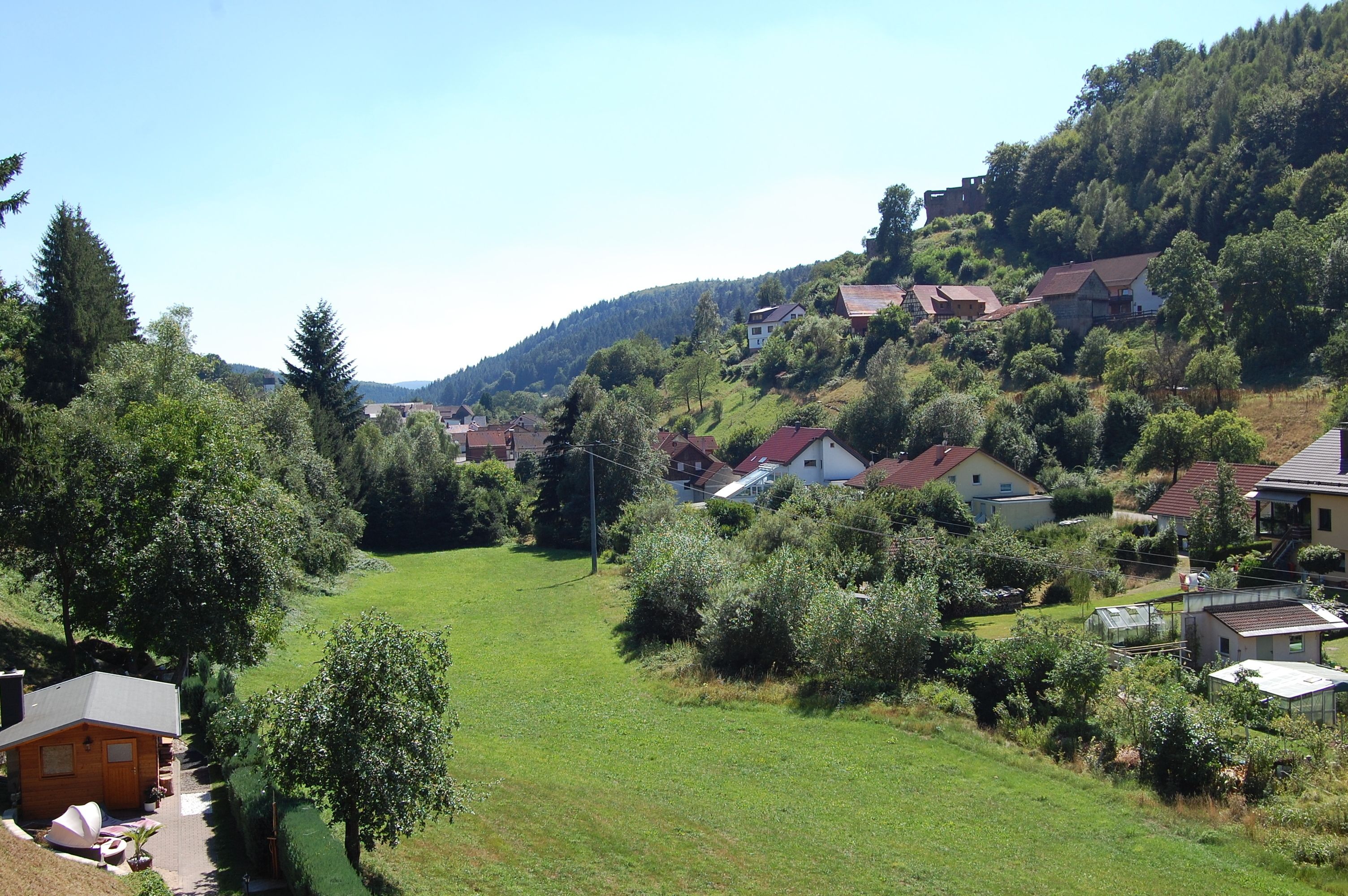Uma aldeia rural com casas numa encosta, rodeada por vegetação e árvores.