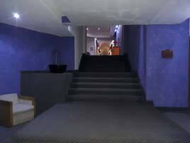 Uma escadaria que dá acesso a um andar superior, uma mesa de recepção e uma área de recepção com uma planta e uma placa na parede.