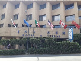 Exterior do InnSur Hotel & Villas com diversas bandeiras, incluindo a bandeira americana, e uma placa indicando a entrada.
