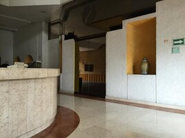 Um lobby com um balcão de recepção de mármore, divisória de vidro e uma placa indicadora verde.