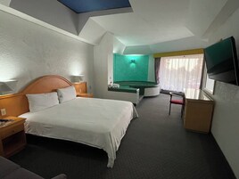 Quarto de hotel com cama, escrivaninha, cadeira, televisão e parede verde.