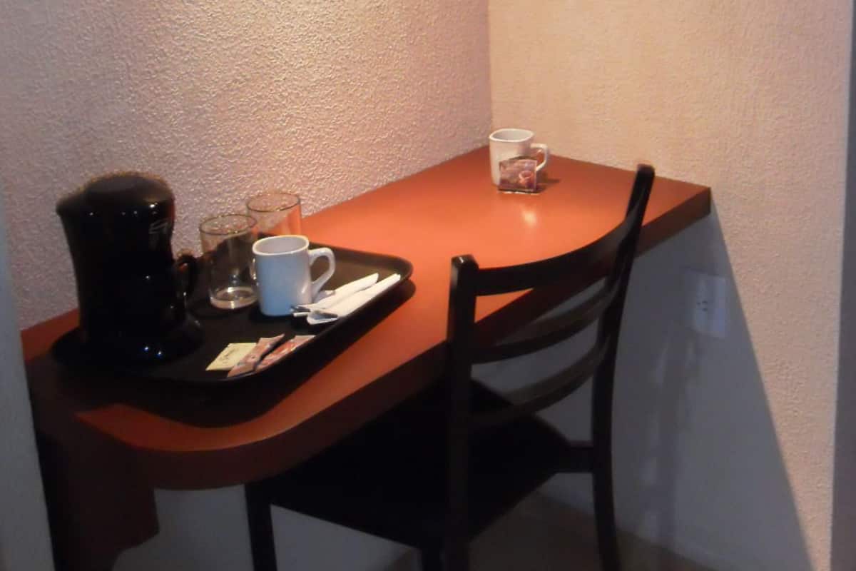 Uma pequena área de refeições com uma mesa, cadeiras, uma máquina de café e uma xícara.