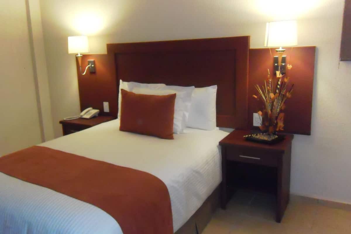 Quarto de hotel com uma cama grande, duas mesas de cabeceira e uma luminária fixada na parede.