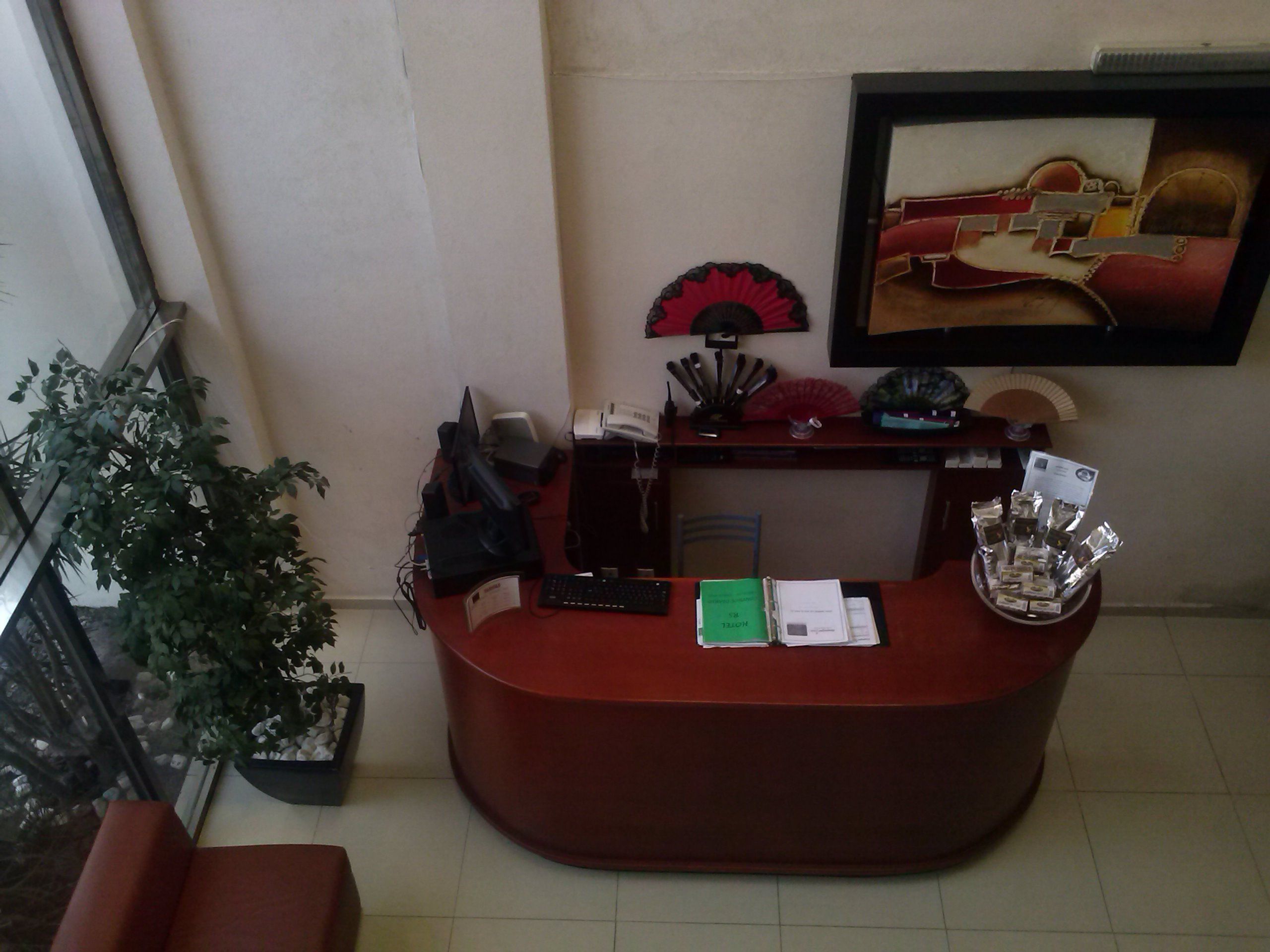 Um balcão de recepção com um computador, um ventilador e uma planta.