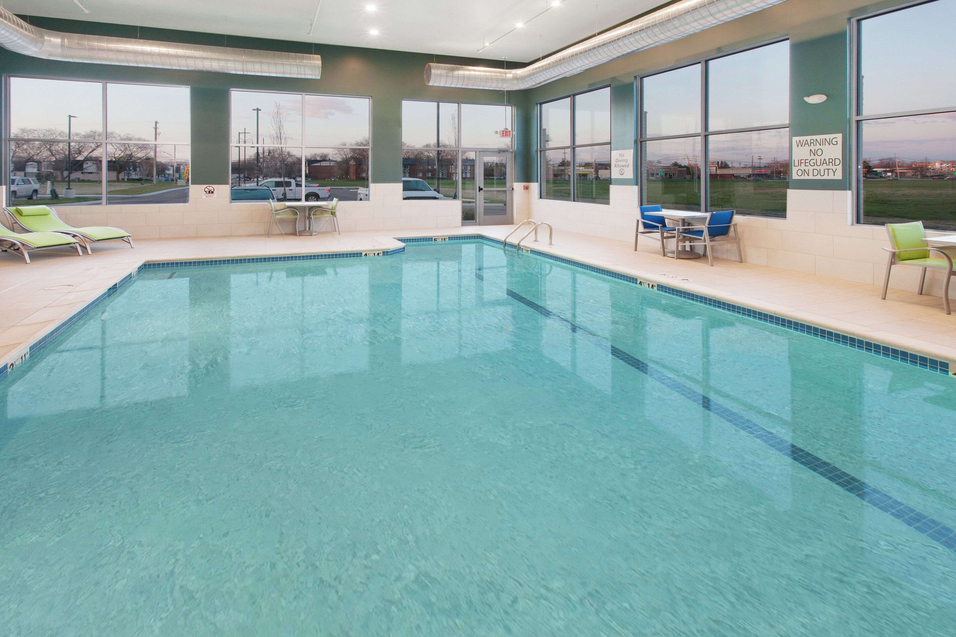 Piscina com água cristalina, rodeada por espreguiçadeiras e uma mesa.