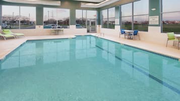 Piscina com água cristalina, rodeada por espreguiçadeiras e uma mesa.