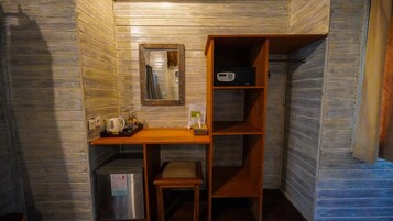 Quarto compacto com painéis de madeira, uma pequena escrivaninha com espelho, geladeira e prateleira com telefone.