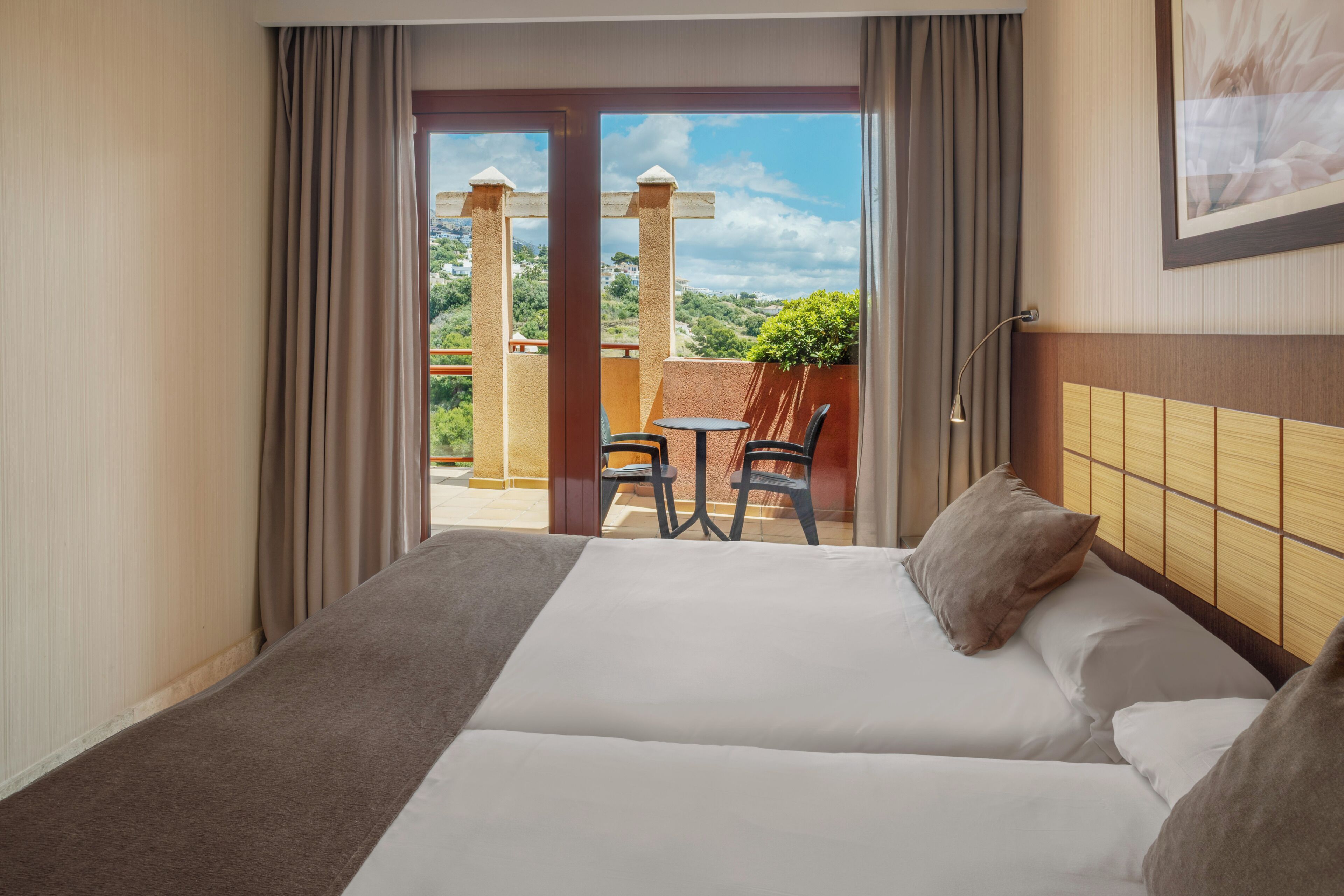 Quarto de hotel com uma cama, uma mesa e cadeiras, e vista para o exterior.
