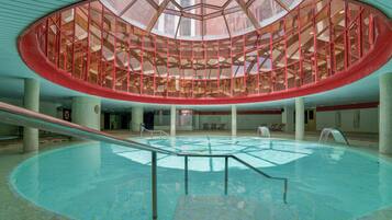 Uma piscina circular com teto de vidro, rodeada por colunas e uma escadaria central.