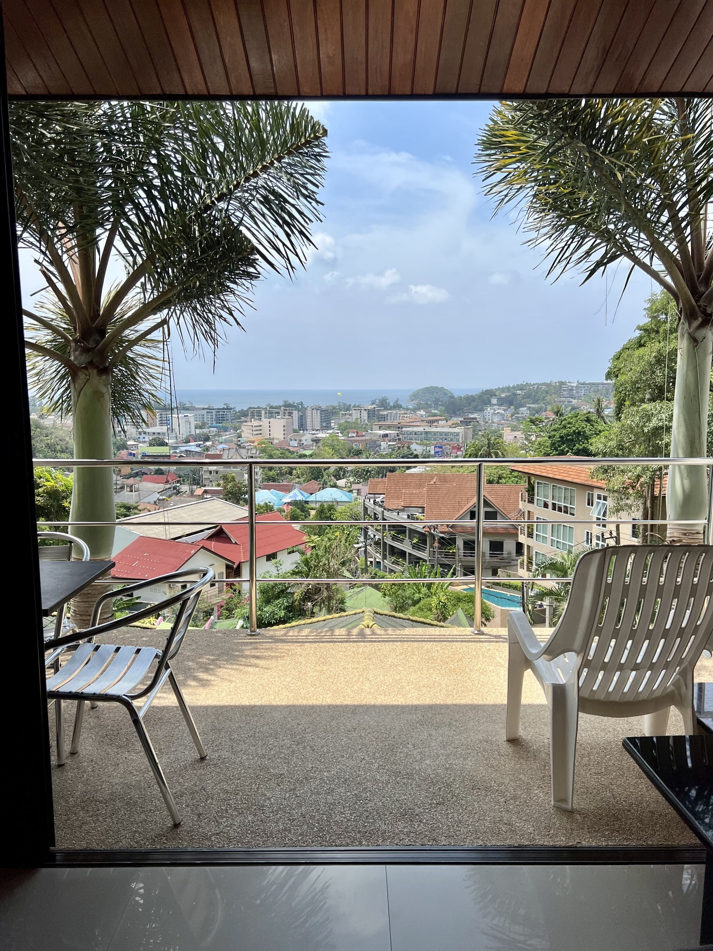 Varanda com duas cadeiras, uma mesa e vista para a paisagem urbana e praia.
