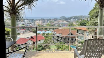 Varanda com duas cadeiras, uma mesa e vista para a paisagem urbana e praia.