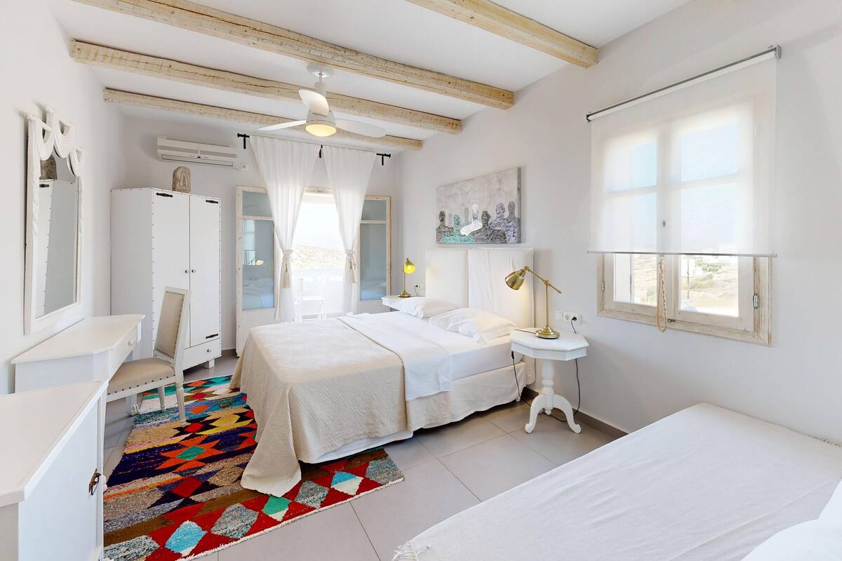 Quarto com cama, mesa de cabeceira, abajur e um tapete colorido.
