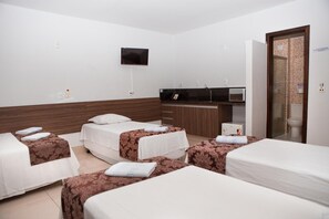 Quarto de hotel com quatro camas, televisão, micro-ondas e casa de banho visível através de uma porta aberta.