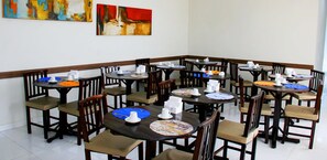 Uma sala de jantar com várias mesas e cadeiras, cada conjunto com pratos, talheres e copos.