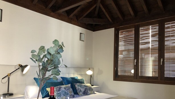 Quarto bem arrumado com cama, luminárias de cabeceira, uma garrafa de vinho e um copo sobre uma mesa.