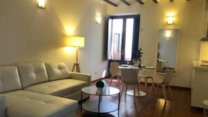 Uma sala de estar com sofá, uma mesa de centro redonda e um espaço de jantar com cadeiras e mesa.