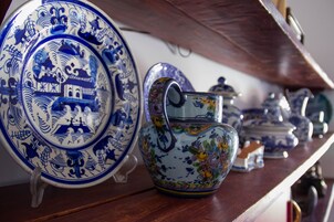 Utensílios de cerâmica em uma prateleira, incluindo um prato e um jarro com motivos florais.