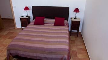 Cama com colcha listrada, duas almofadas vermelhas e duas mesas de cabeceira com abajures.