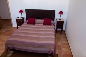 Cama com colcha listrada, duas almofadas vermelhas e duas mesas de cabeceira com abajures.