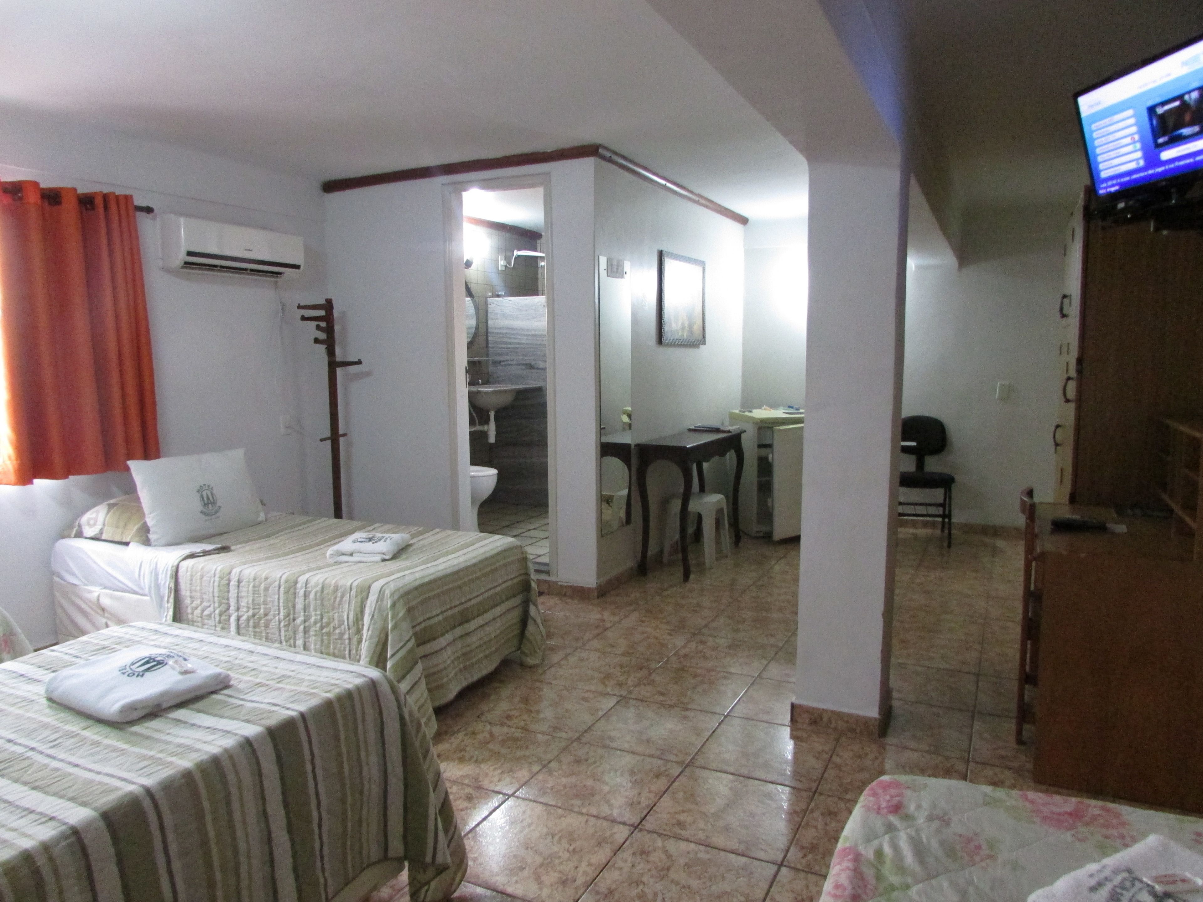 Quarto de hotel com duas camas, uma escrivaninha, uma cadeira e uma televisão.