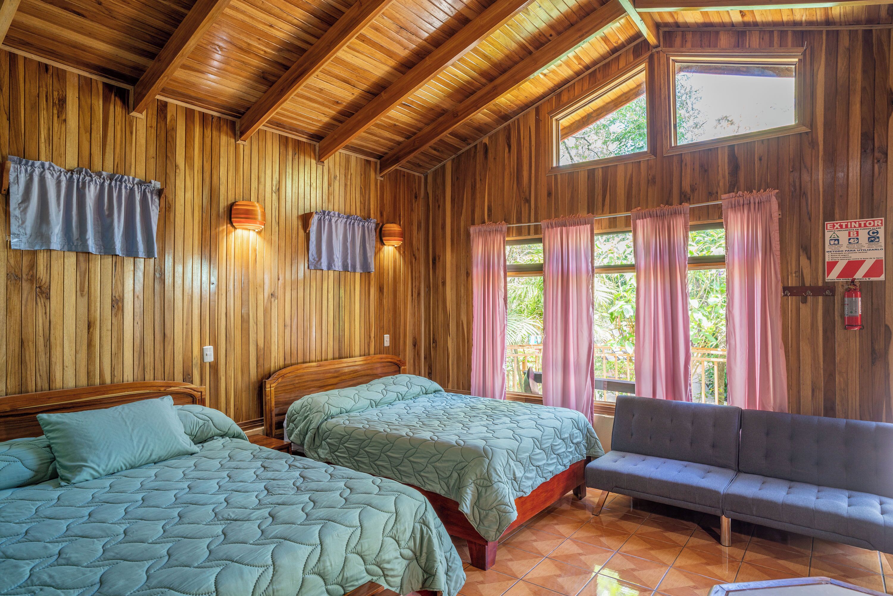 Uma cabana de madeira com duas camas, um sofá e uma janela com cortinas.