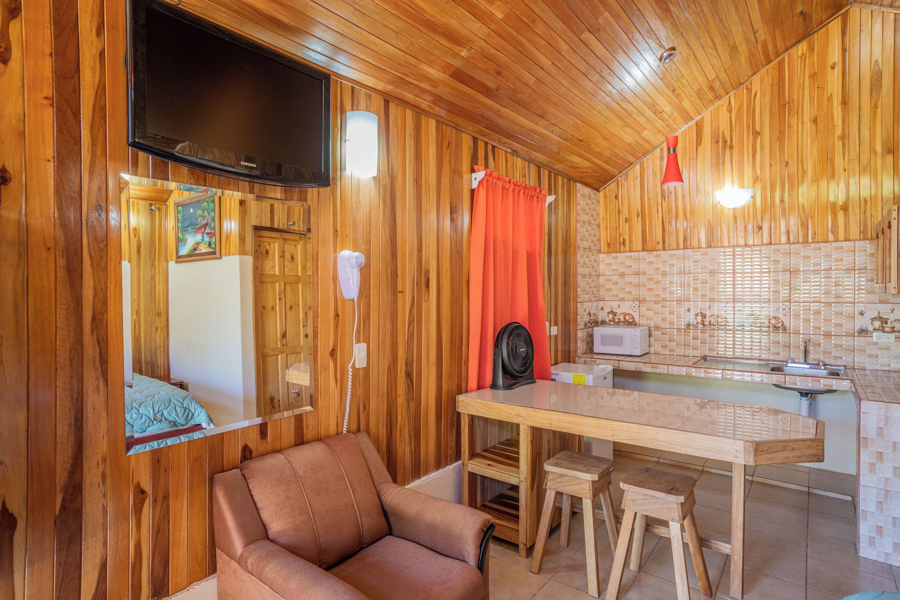 Interior em madeira com um sofá, uma mesa de jantar e uma cozinha equipada com pia e micro-ondas.
