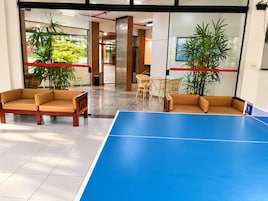 Quarto com mesa de ping pong, dois sofás e plantas em vasos.