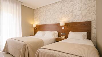 Quarto de hotel com duas camas, cabeceira de madeira, abajures e papel de parede estampado.