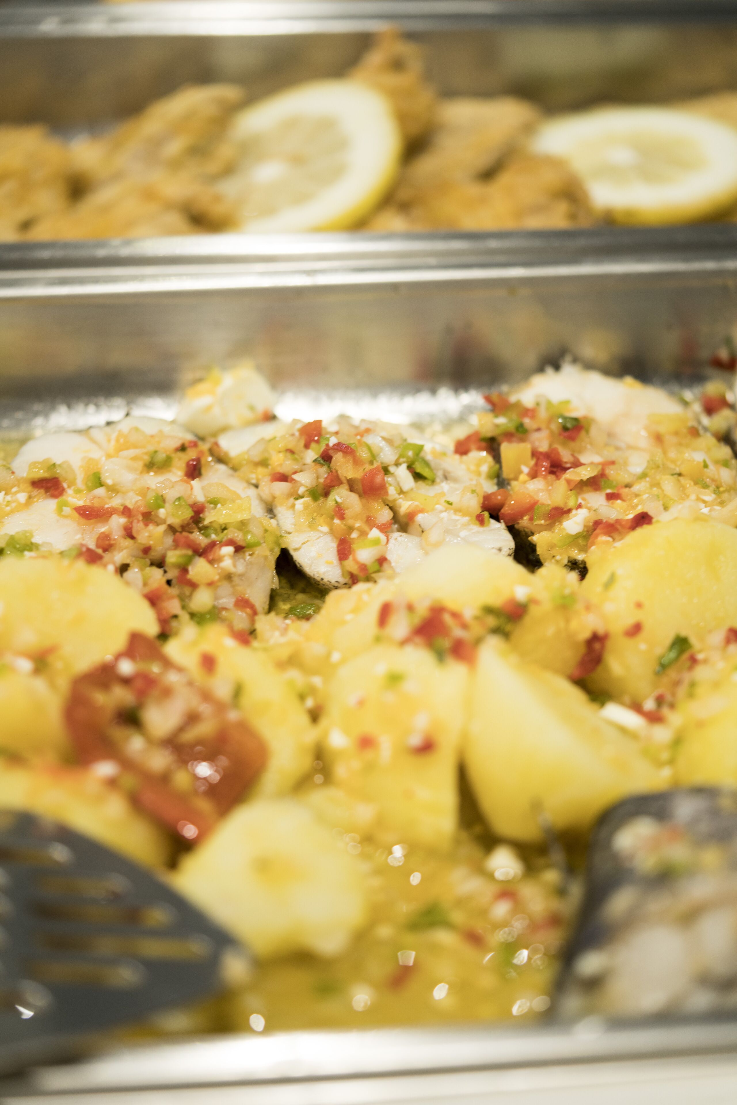 Buffet com diversos pratos, incluindo peixe, batatas e uma salada com legumes picados.