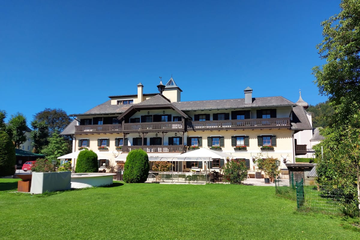 Um edifício grande, de vários andares, com arquitetura tradicional, com varandas e um jardim bem cuidado na frente.