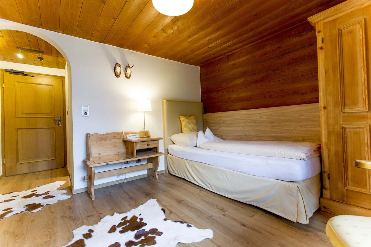 Quarto de cabana de madeira com cama, mesa de cabeceira, abajur e tapete de couro de vaca.
