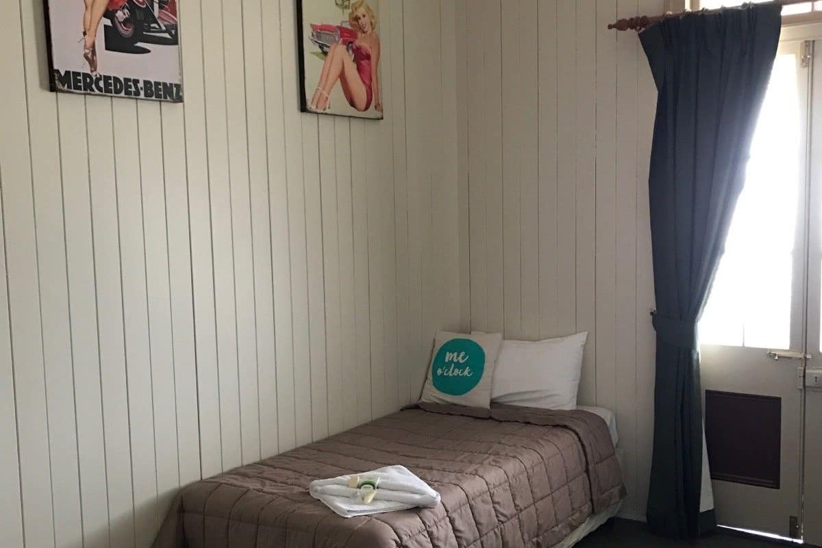 Quarto com uma cama, uma janela com cortinas, uma parede com dois cartazes e uma mesinha.