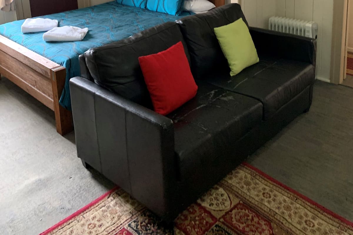 Quarto com cama de madeira, sofá de couro preto, colcha azul e branca e um espelho na parede.