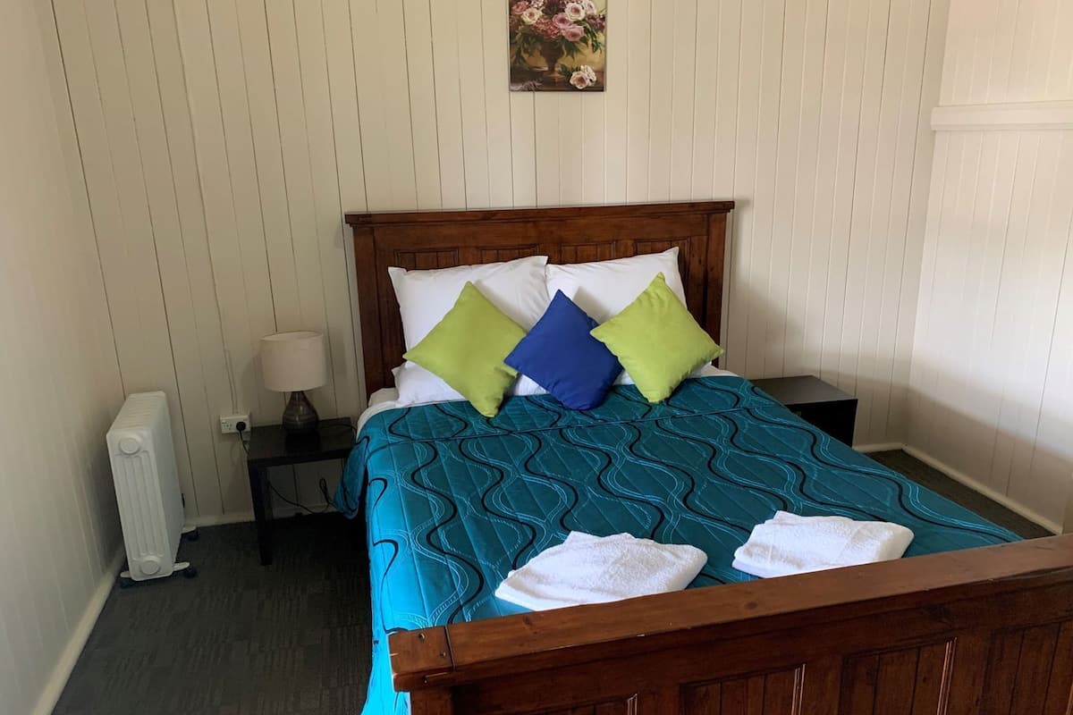 Uma cama bem arrumada com colcha estampada, cabeceira de madeira e mesa de cabeceira com abajur.