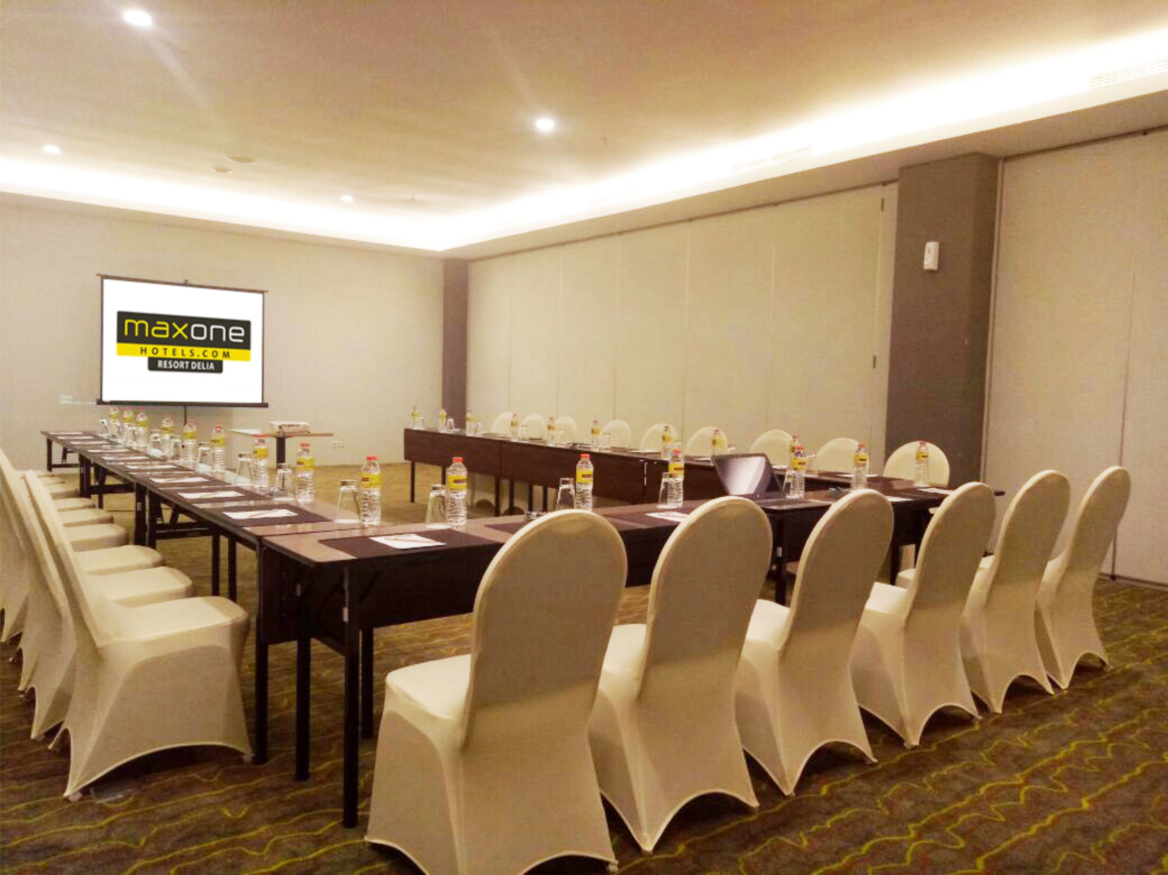 Uma sala de conferências com uma mesa comprida, cadeiras e uma tela de projeção exibindo o nome de um hotel.