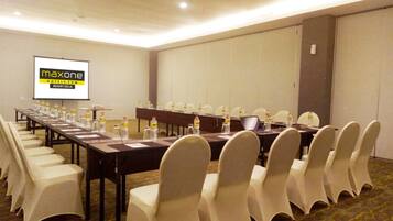 Uma sala de conferências com uma mesa comprida, cadeiras e uma tela de projeção exibindo o nome de um hotel.