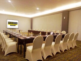 Uma sala de conferências com uma mesa comprida, cadeiras e uma tela de projeção exibindo o nome de um hotel.