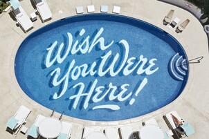 Piscina com um grande letreiro que diz 'Wish You Were Here!'