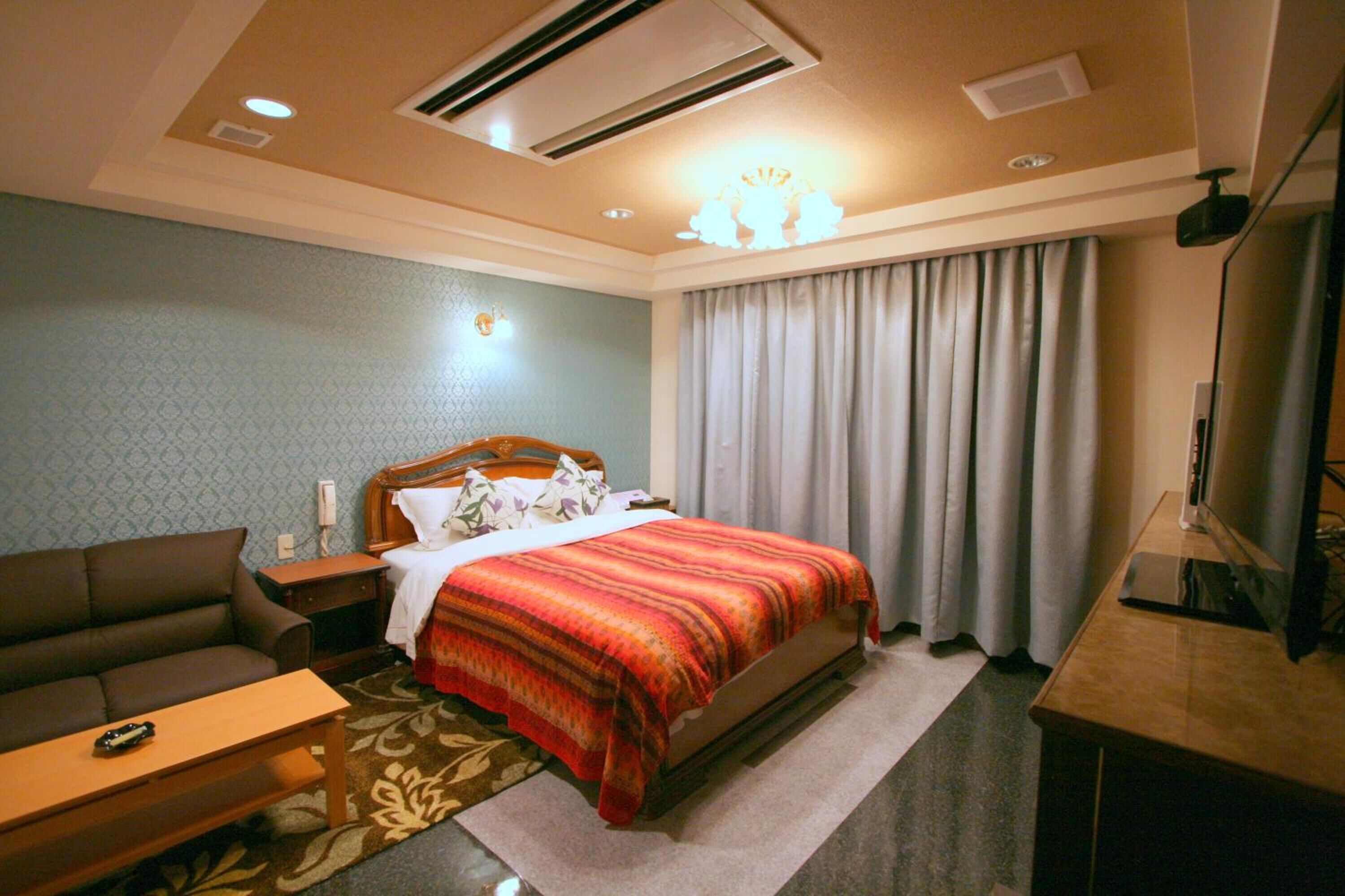 Quarto de hotel com cama, sofá, escrivaninha e televisão.
