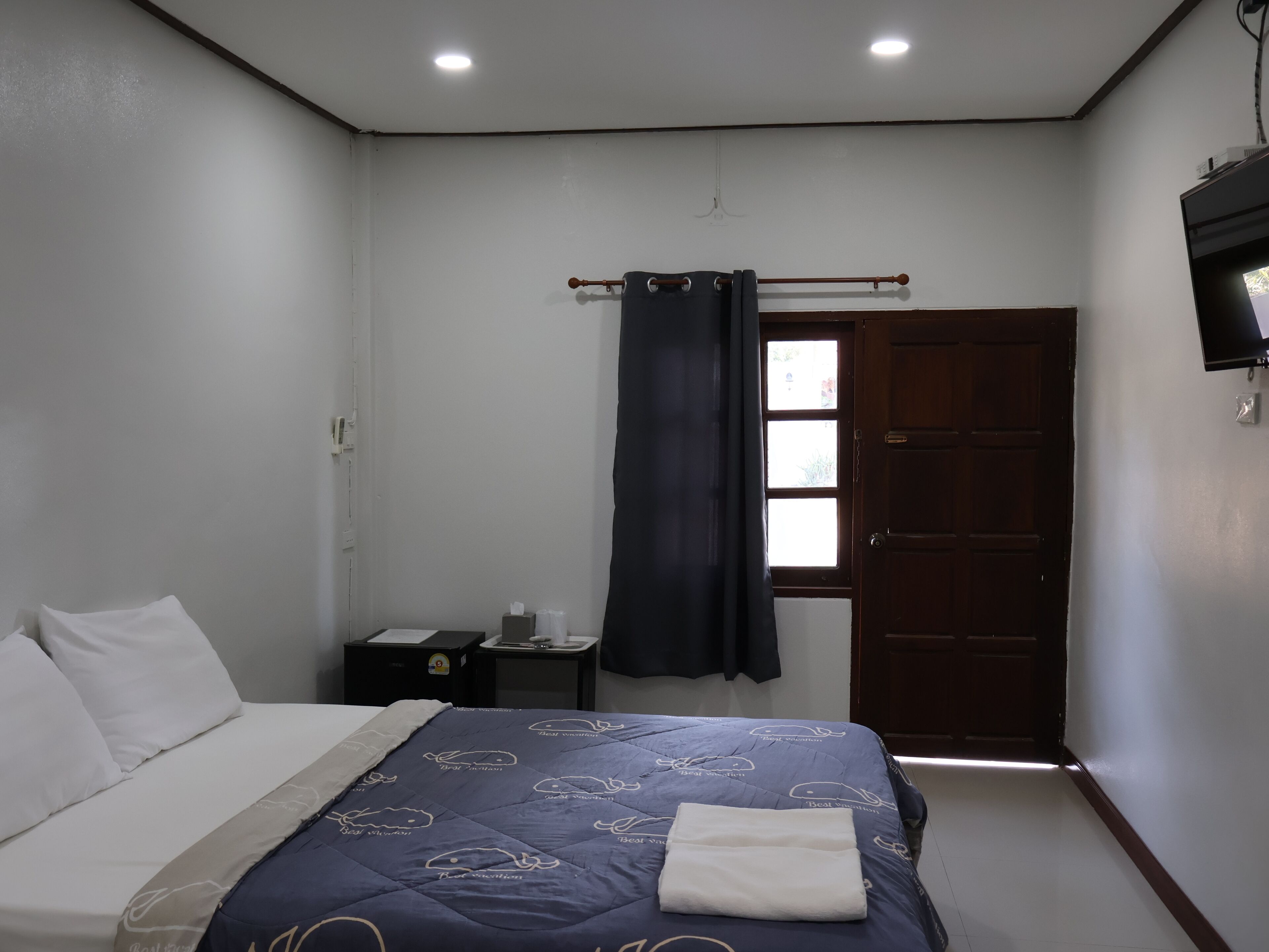 Quarto com cama, mesa de cabeceira, janela com cortinas e porta.