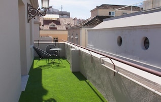 Terraço no telhado com grama sintética, guarda-corpo de metal e um par de cadeiras.