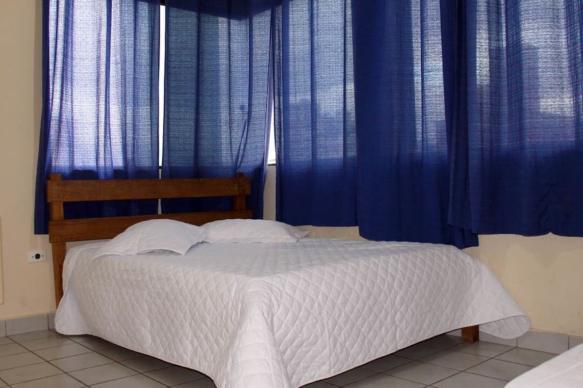 Uma cama com cabeceira de madeira, roupa de cama branca e cortinas azuis.