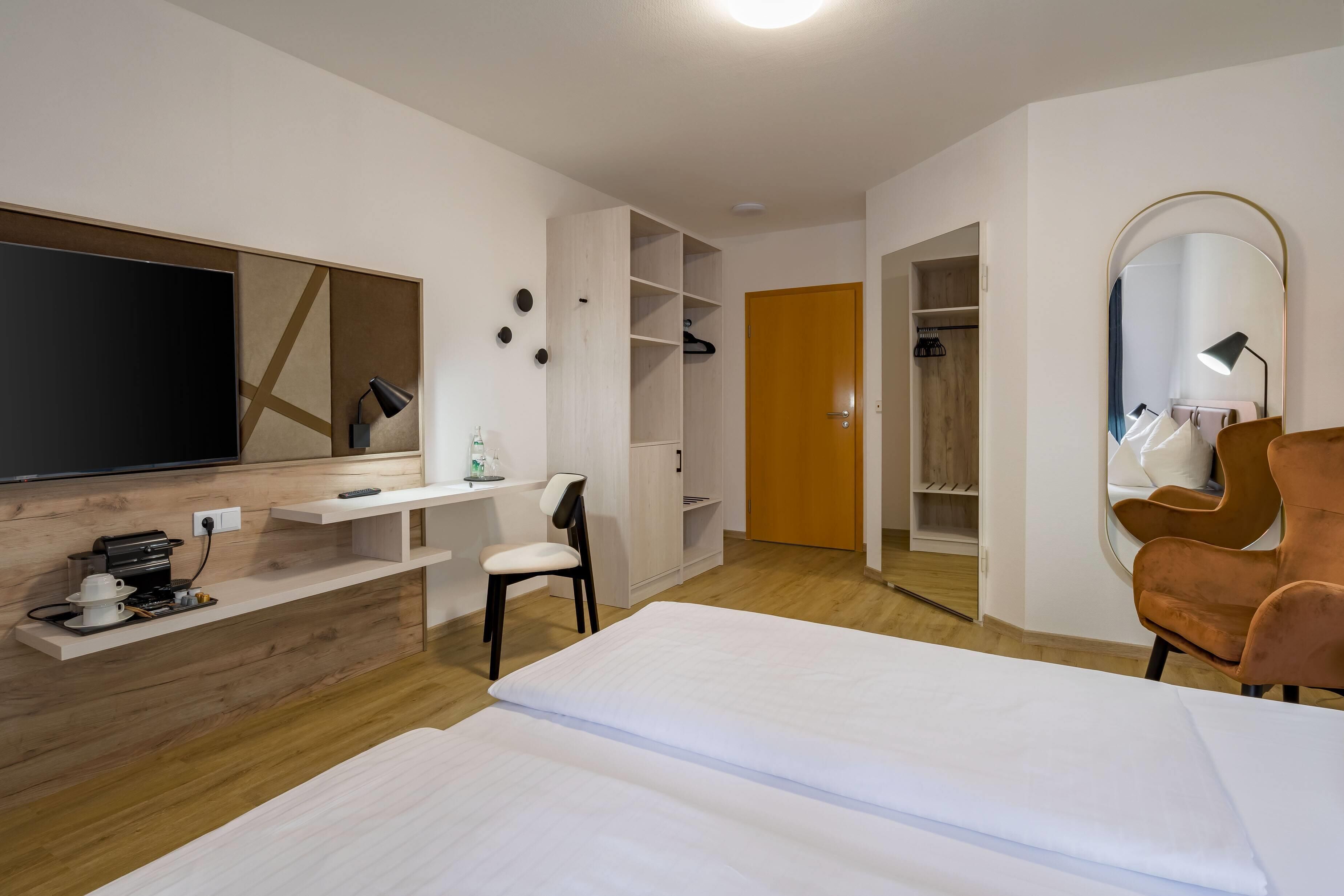 Quarto moderno com cama, televisão, escrivaninha, cadeira, guarda-roupa e espelho.