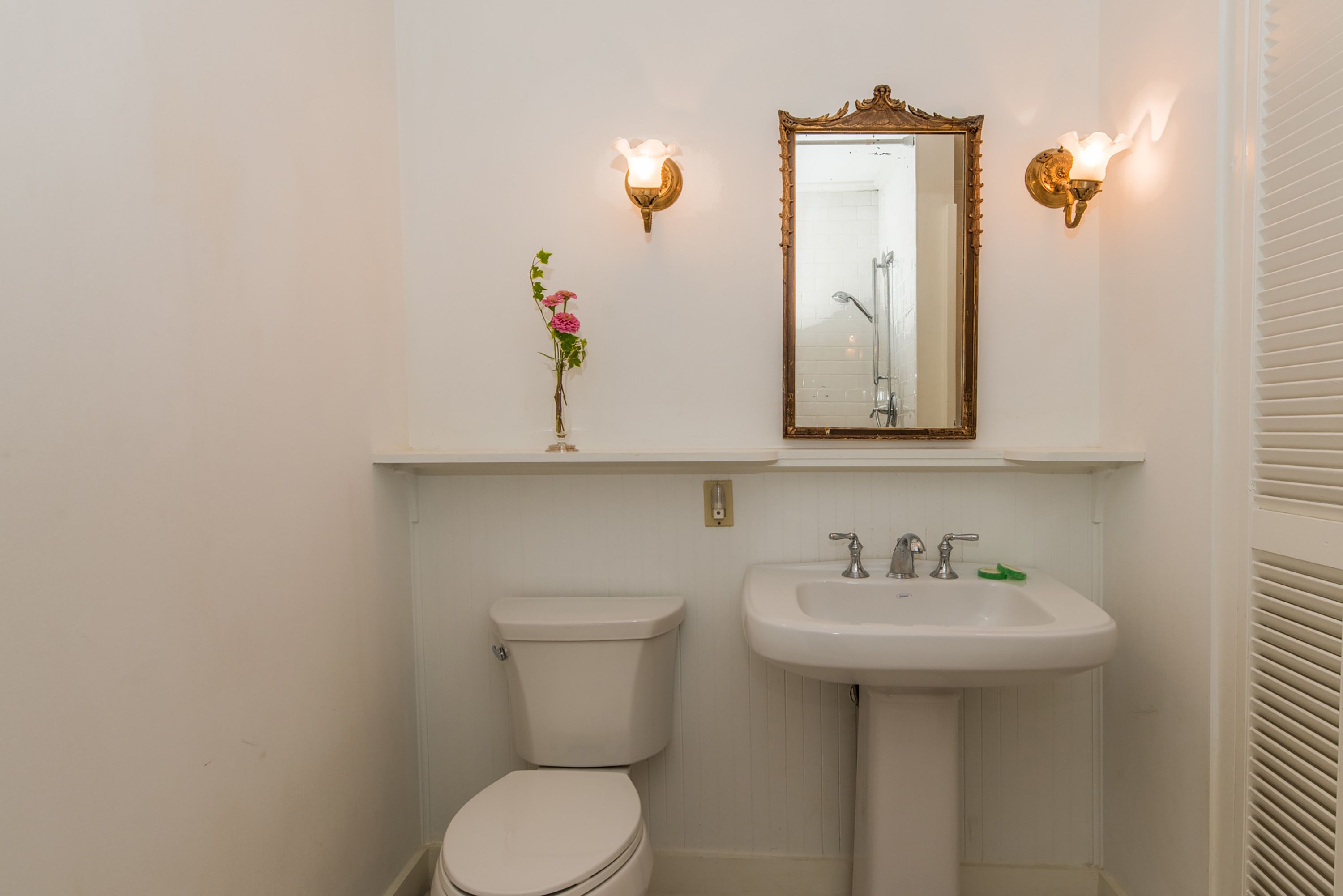 Casa de banho com sanita, lavatório e espelho com candeeiros de parede.